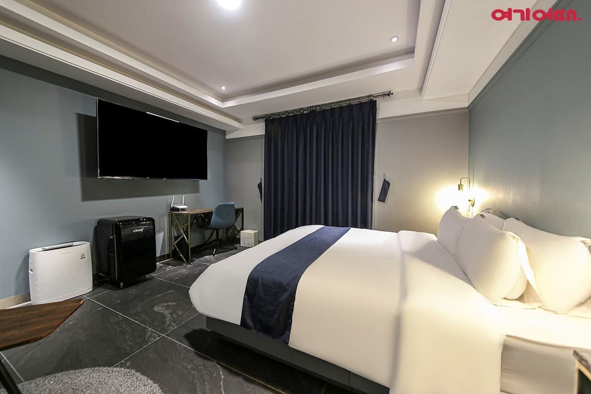 Quarto de hotel moderno com uma cama grande, televisão de tela plana, escrivaninha com cadeira e aquecedor.