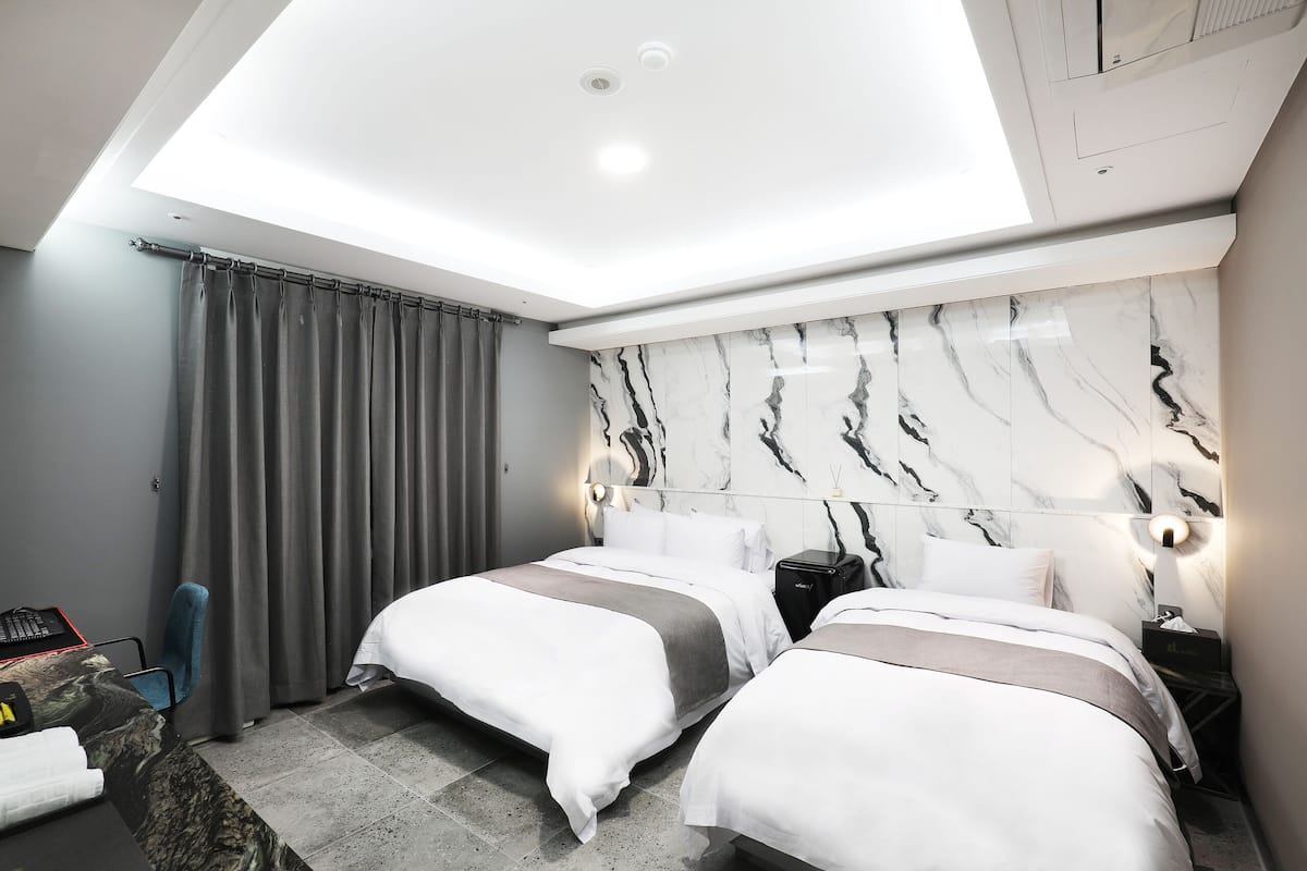 Quarto de hotel moderno com duas camas, uma escrivaninha e uma luminária de teto.