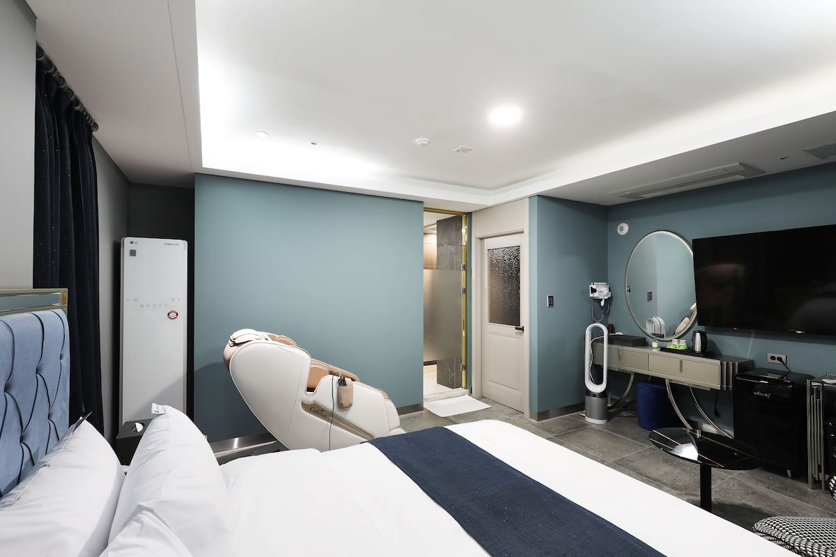 Quarto de hotel com cama, cadeira de massagem, televisão, escrivaninha com espelho e minibar.