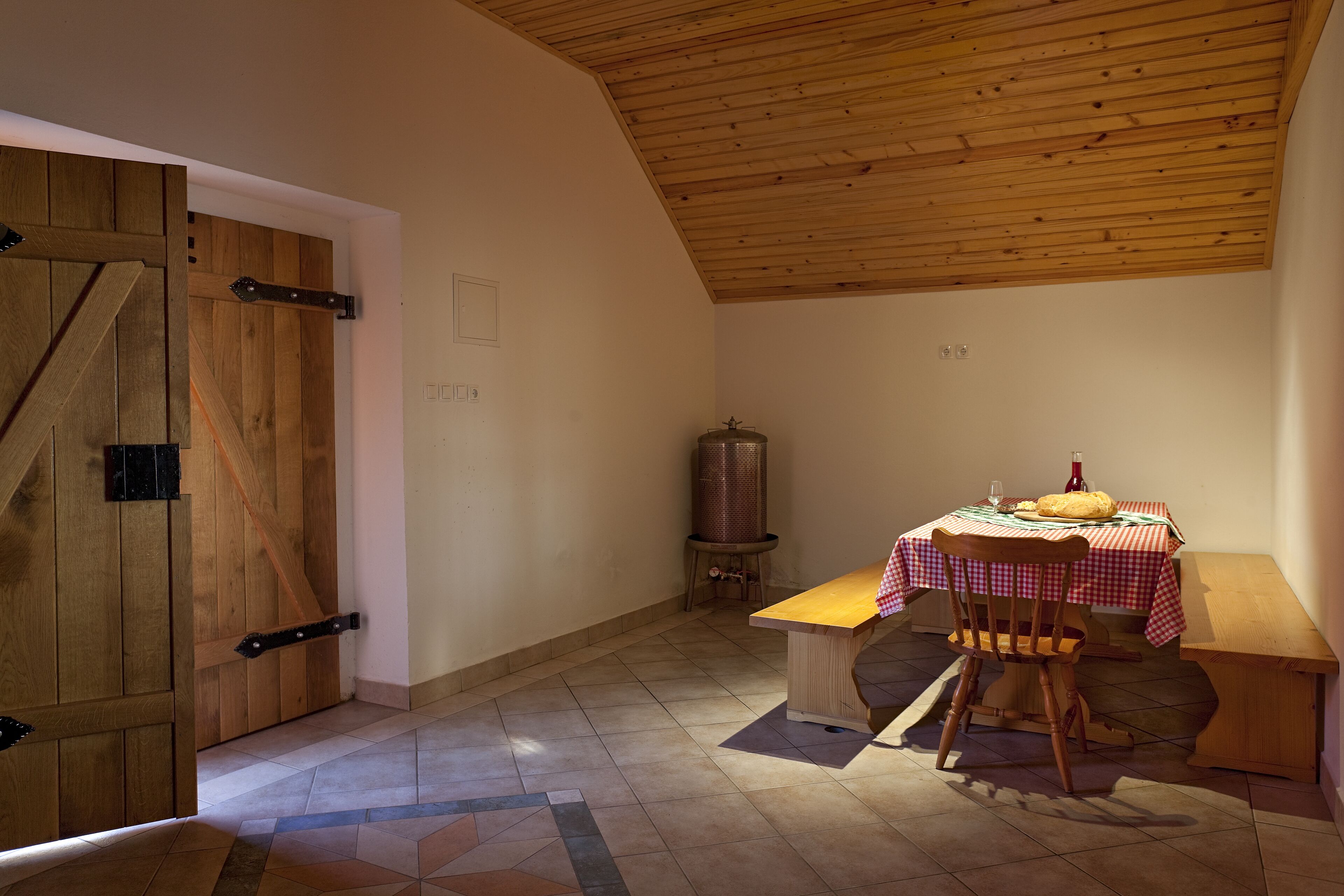 Um quarto com porta de madeira, uma mesa com toalha xadrez, um banco e teto rústico.