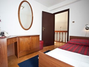 Quarto com cômoda de madeira, cama com roupa de cama xadrez, espelho e porta que dá para uma varanda.