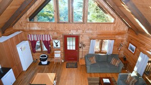 Uma cabana acolhedora com interior de madeira, uma porta vermelha, um sofá e um espaço de jantar.