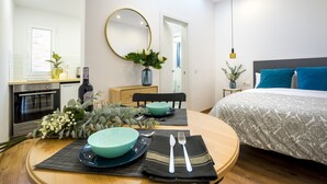 Quarto de hotel moderno com área de refeições, cama com almofadas azuis e cozinha.