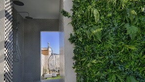 Casa de banho com chão xadrez, zona de duche e parede verde com plantas.