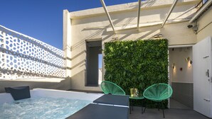Área de piscina no terraço com hidromassagem, duas cadeiras verdes e uma parede coberta de vegetação.