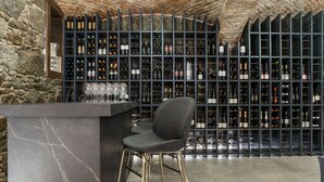 Uma adega com área de bar, paredes de pedra e uma estante de vinhos cheia de garrafas.