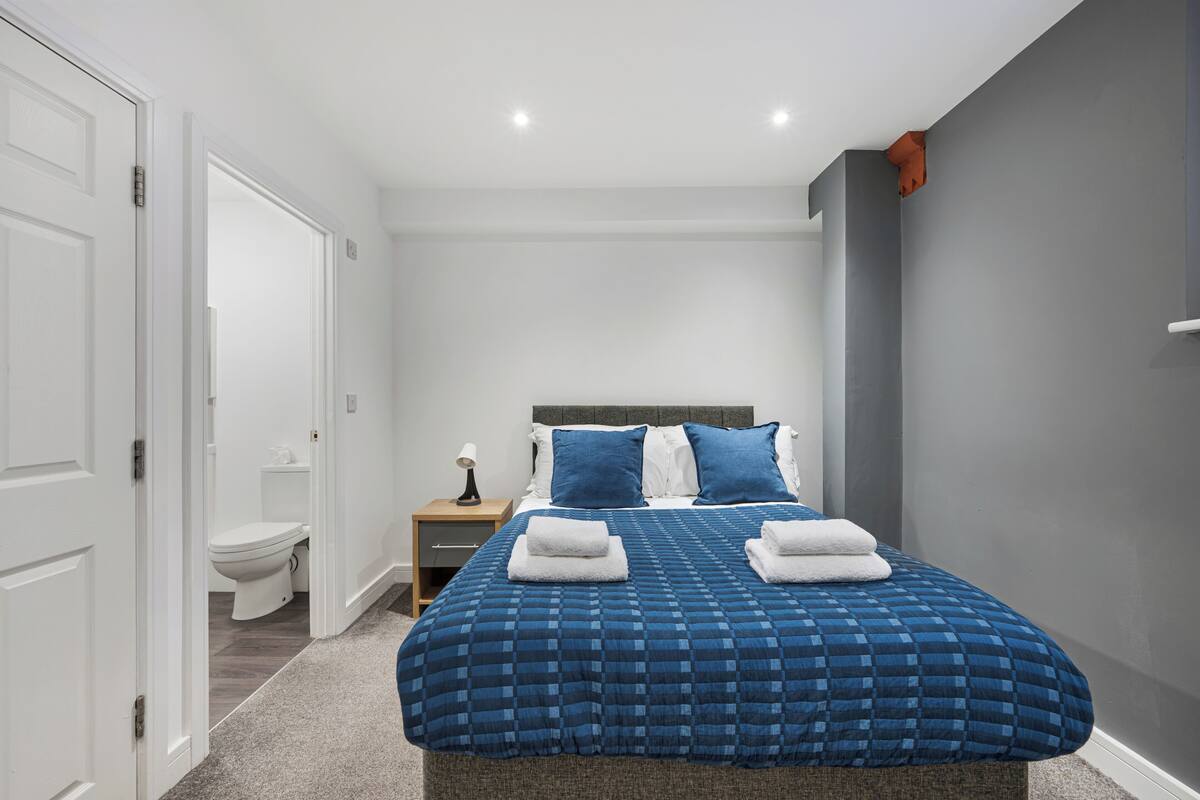 Quarto com uma cama, mesa de cabeceira, luminária e banheiro com vaso sanitário.