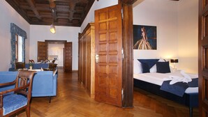 Quarto de hotel com teto de madeira, cama com cabeceira azul, um quadro na parede e uma porta de madeira.