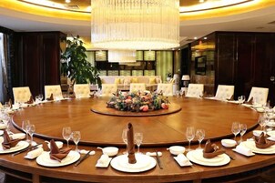 Mesa de jantar redonda posta para uma refeição formal, com cadeiras ao redor.