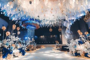 Espaço interno com palco central, elementos decorativos pendurados e arranjos florais.