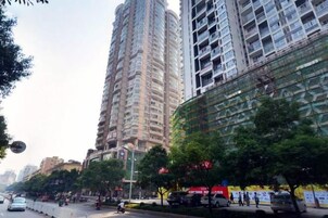 Um edifício alto com vários andares, uma rua com árvores e veículos estacionados, e um canteiro de obras com andaimes.