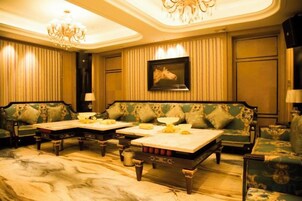 Quarto com lustre, sofás estofados verdes, piso de mármore e um quadro emoldurado na parede.