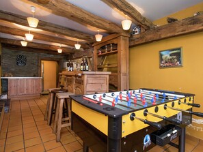 Um quarto com mesa de pebolim, bar de madeira, alvo de dardos e mesa de bilhar.