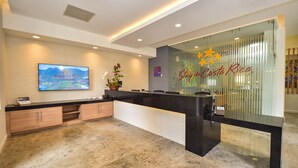 Uma área de recepção com balcão preto, TV fixada na parede e parede de vidro com a placa 'Stay in Costa Rica'.