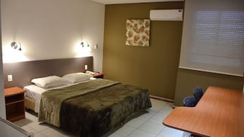 Quarto de hotel com cama, mesas de cabeceira, escrivaninha e tela de projetor.