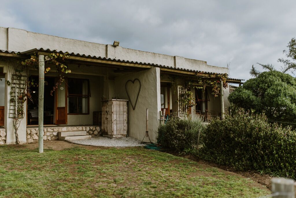 Uma casa com varanda coberta, decoração em formato de coração na parede e área de jardim.