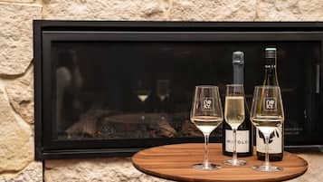 Uma mesa de madeira com duas taças e duas garrafas de vinho, em frente a uma parede de pedra e uma lareira.