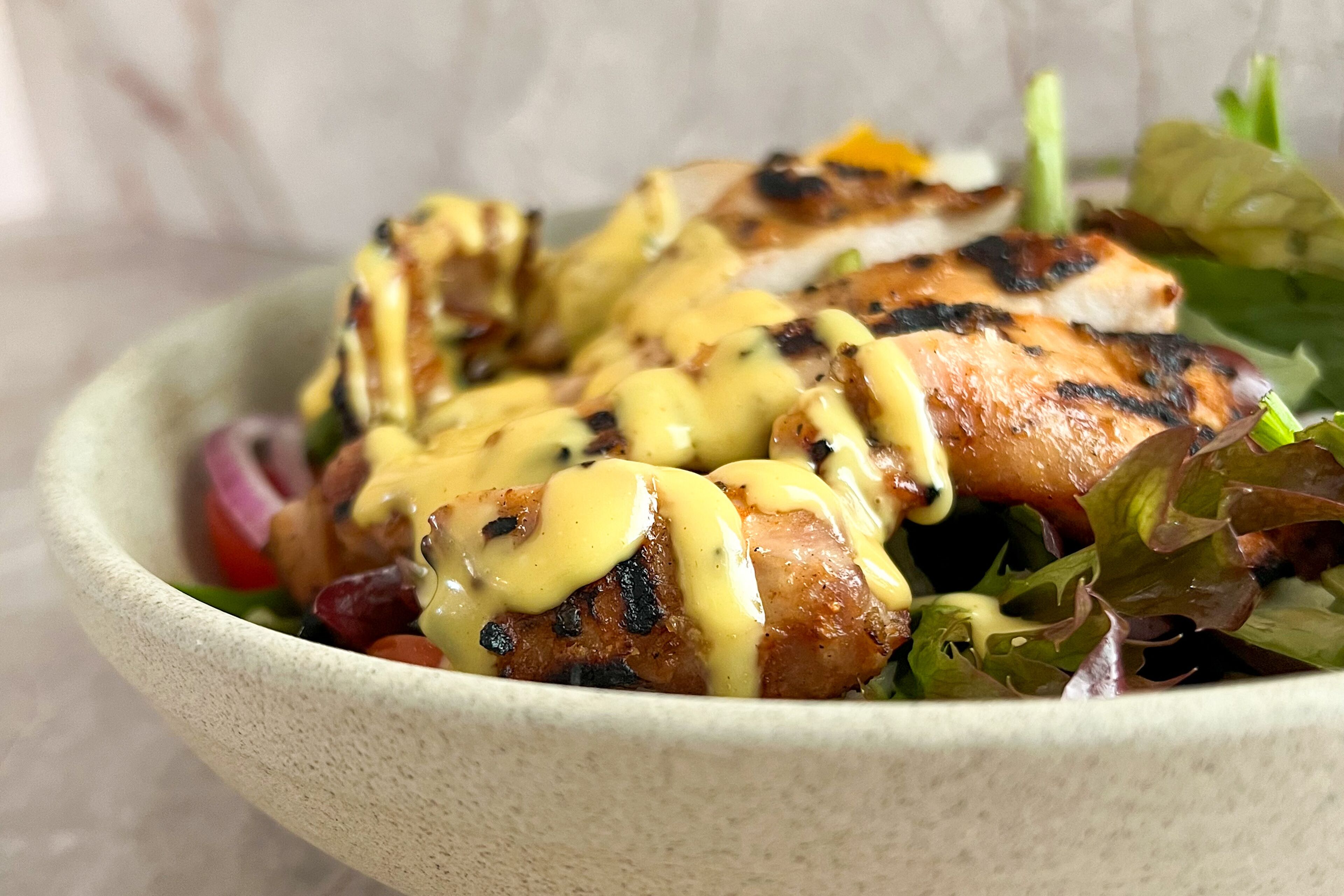 Uma tigela de frango grelhado com molho cremoso, acompanhada de uma salada.