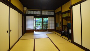 Um quarto japonês tradicional com piso de tatame, portas deslizantes e vista para o verde lá fora.