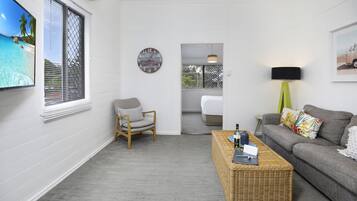 Uma sala de estar moderna com um sofá cinzento, uma mesa de centro de vime, uma cadeira de madeira e uma televisão exibindo uma cena de praia.