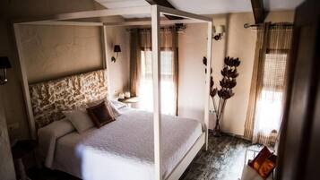 Uma cama de dossel com cabeceira em padrão de pedra, mesa de cabeceira com abajur e um vaso com flores.