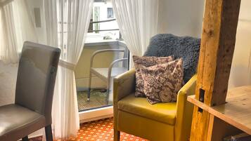 Um quarto com uma poltrona amarela, uma cadeira cinza e uma janela com cortinas brancas.