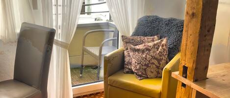 Um quarto com uma poltrona amarela, uma cadeira cinza e uma janela com cortinas brancas.