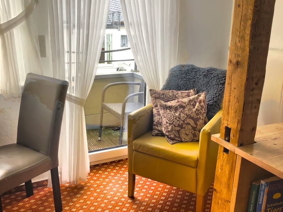 Um quarto com uma poltrona amarela, uma cadeira cinza e uma janela com cortinas brancas.