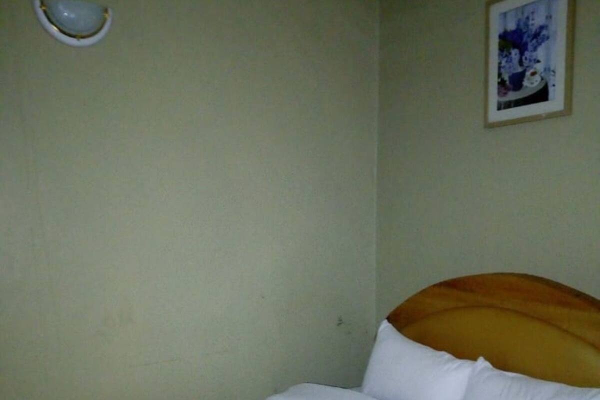Cama com cabeceira de madeira e roupa de cama branca em quarto com parede lisa e quadro emoldurado.