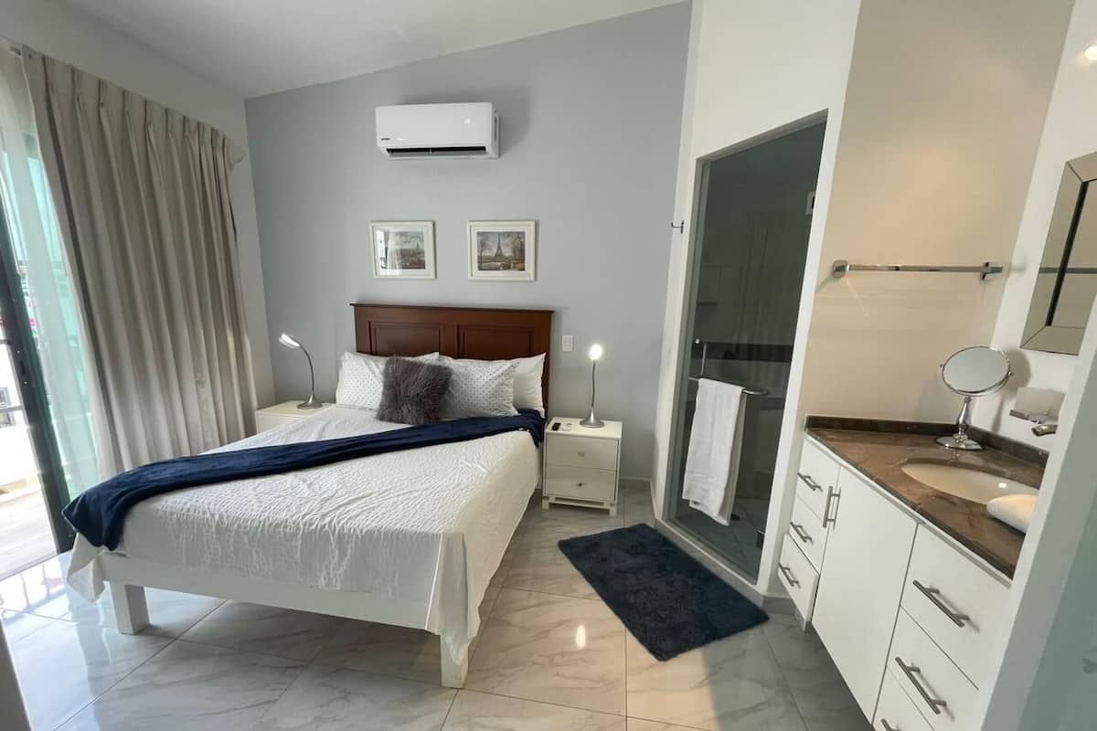 Quarto moderno com uma cama grande, mesas de cabeceira, um closet espaçoso e um banheiro com chuveiro e pia.