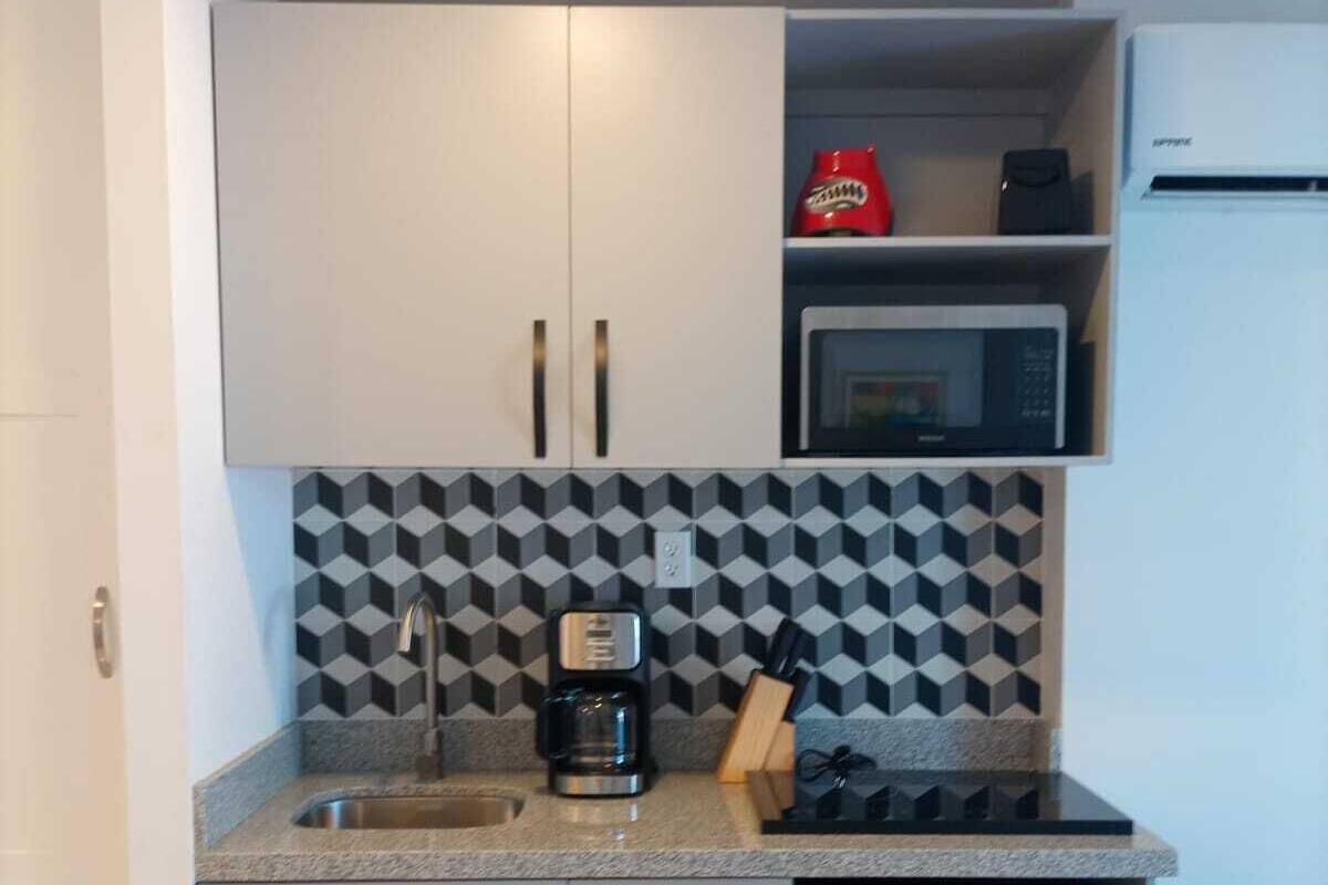 Uma cozinha compacta com micro-ondas, cafeteira e um frigorífico pequeno.