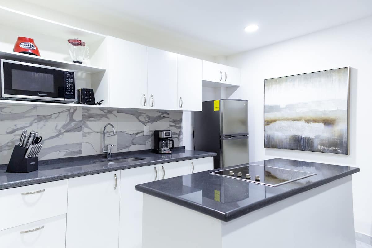 Cozinha moderna com armários brancos, painel de fundo de mármore, bancada preta, micro-ondas, cafeteira, geladeira e pia.