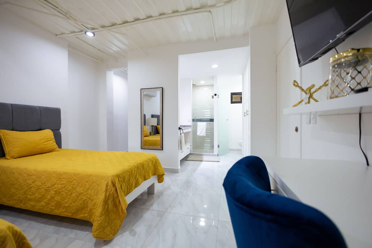 Quarto de hotel com uma cama, uma cadeira, uma televisão e um banheiro visível ao fundo.