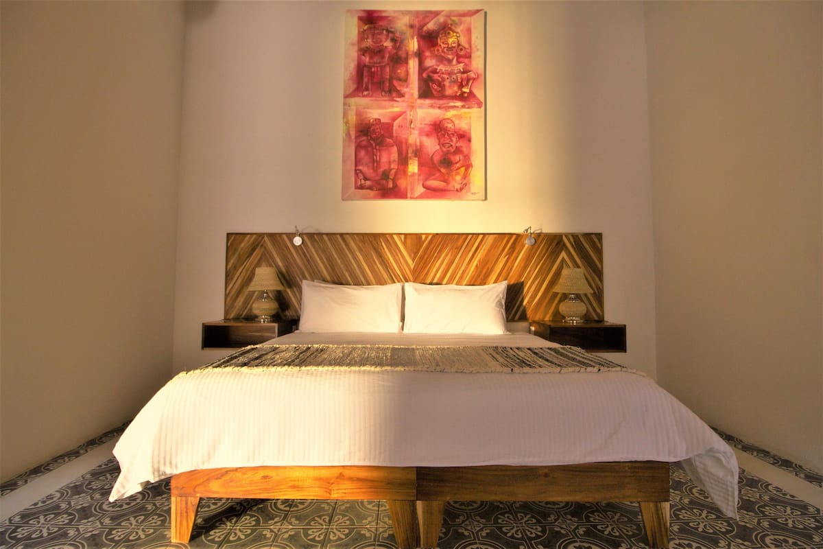 Cama bem arrumada com cabeceira de madeira, uma obra de arte na parede e piso estampado.