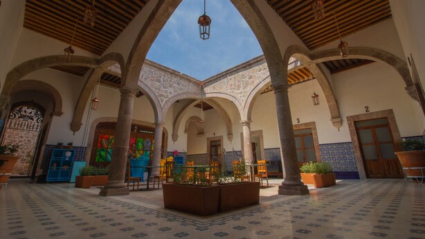 Um pátio interno com arcos de pedra, piso de azulejos e plantas em vasos.