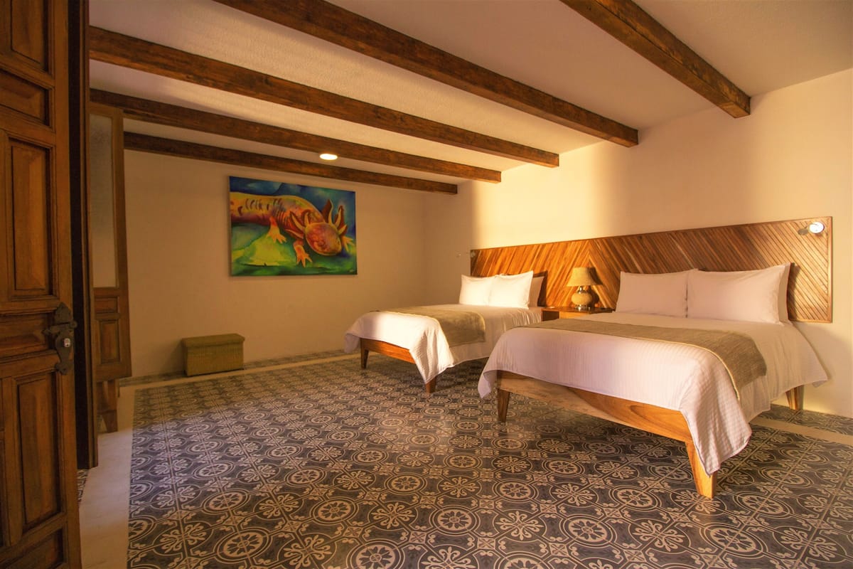 Quarto de hotel com duas camas, teto de madeira, ladrilhos com padrão e um quadro na parede.