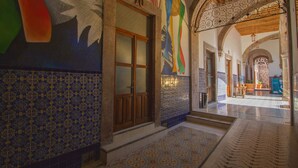 Um corredor com azulejos estampados, portas de madeira e um mural colorido.