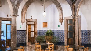 Um interior com arcos de pedra, portas numeradas, paredes azulejadas e mesas e cadeiras de madeira.