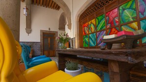 Interior vibrante com janelas de vitrais coloridas, um banco de madeira com saboneteiras e assentos em amarelo e azul.