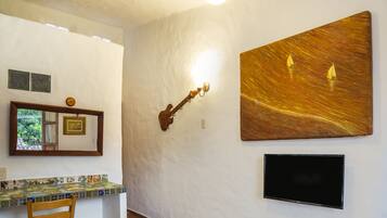 Quarto com mesa azulejada, cadeira de madeira, arte de parede com um violão, uma pintura e uma televisão.