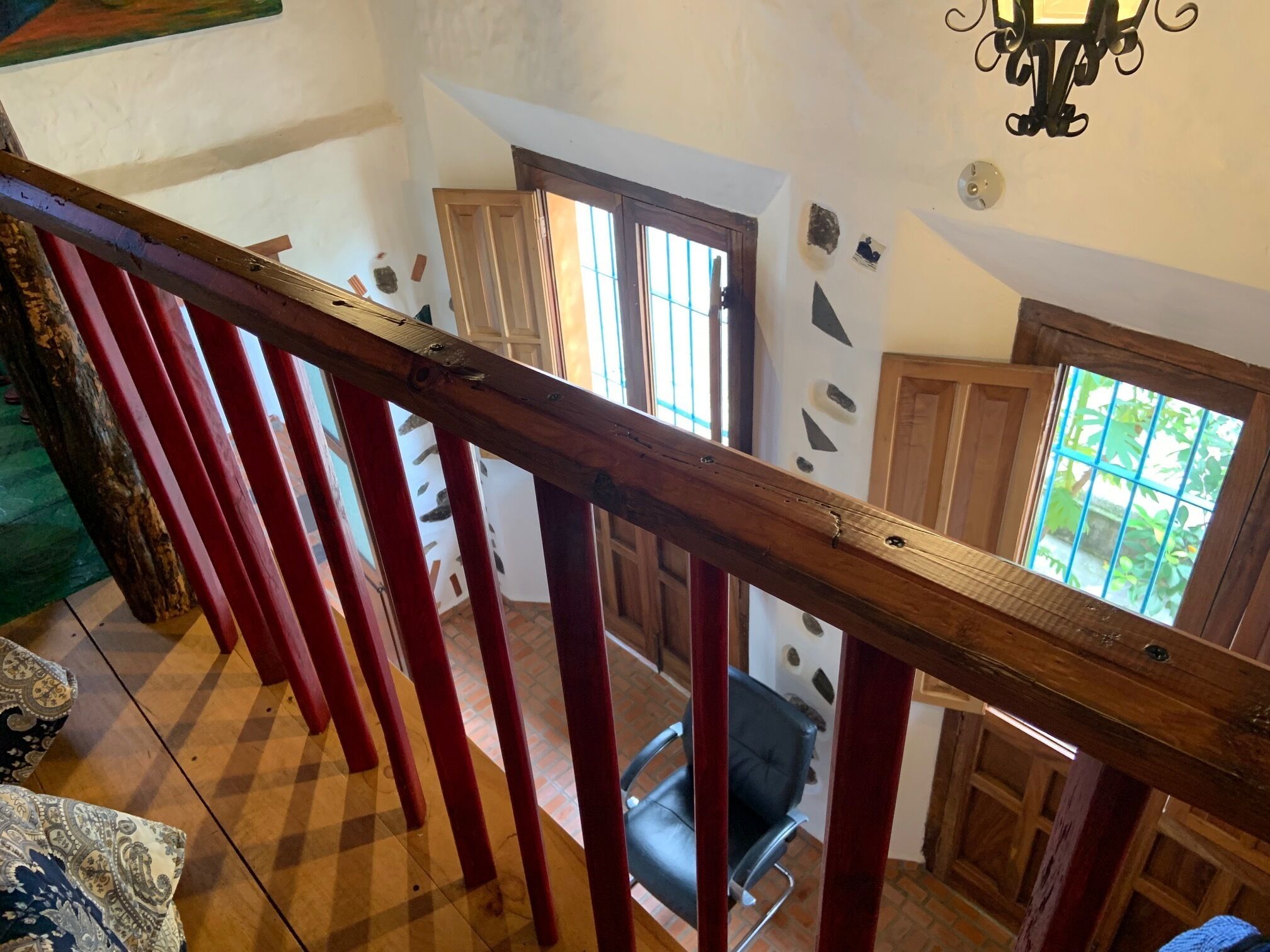 Uma escadaria com corrimão de madeira, piso xadrez e vista para um quarto com janela e porta.