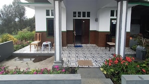 Uma área externa coberta com piso de azulejos, uma mesa pequena e cadeiras.