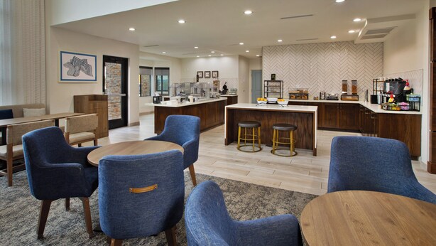 Um hall de hotel moderno com área de bar, espaços de estar e parede com padrão losango.