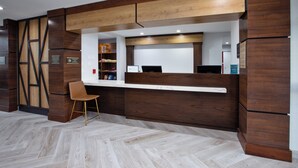 Uma área de recepção com um balcão de madeira, uma cadeira marrom e um piso em padrão herringbone.