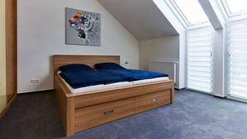 Quarto com teto inclinado, cama com estrutura de madeira, radiador e claraboia.