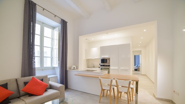 Uma sala de estar moderna com uma mesa de centro de vidro, um sofá com almofadas vermelhas e uma área de jantar com cadeiras de madeira.