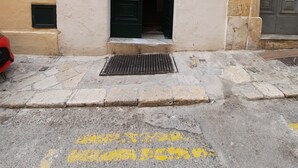 Entrada de um edifício com porta verde, uma pequena janela e uma grade de metal no pavimento.