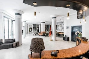 Um lobby moderno com um balcão de recepção curvo, áreas de estar e uma escada ao fundo.