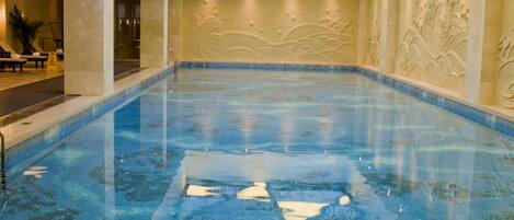 Uma grande piscina coberta com teto de vidro, rodeada por paredes com desenhos de ondas.