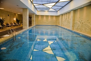 Piscina interior com água cristalina, chão ladrilhado e teto com claraboia.